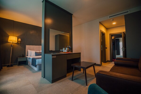Quarto de hotel com cama, mesa de cabeceira, luminária, escrivaninha, espelho e sofá.