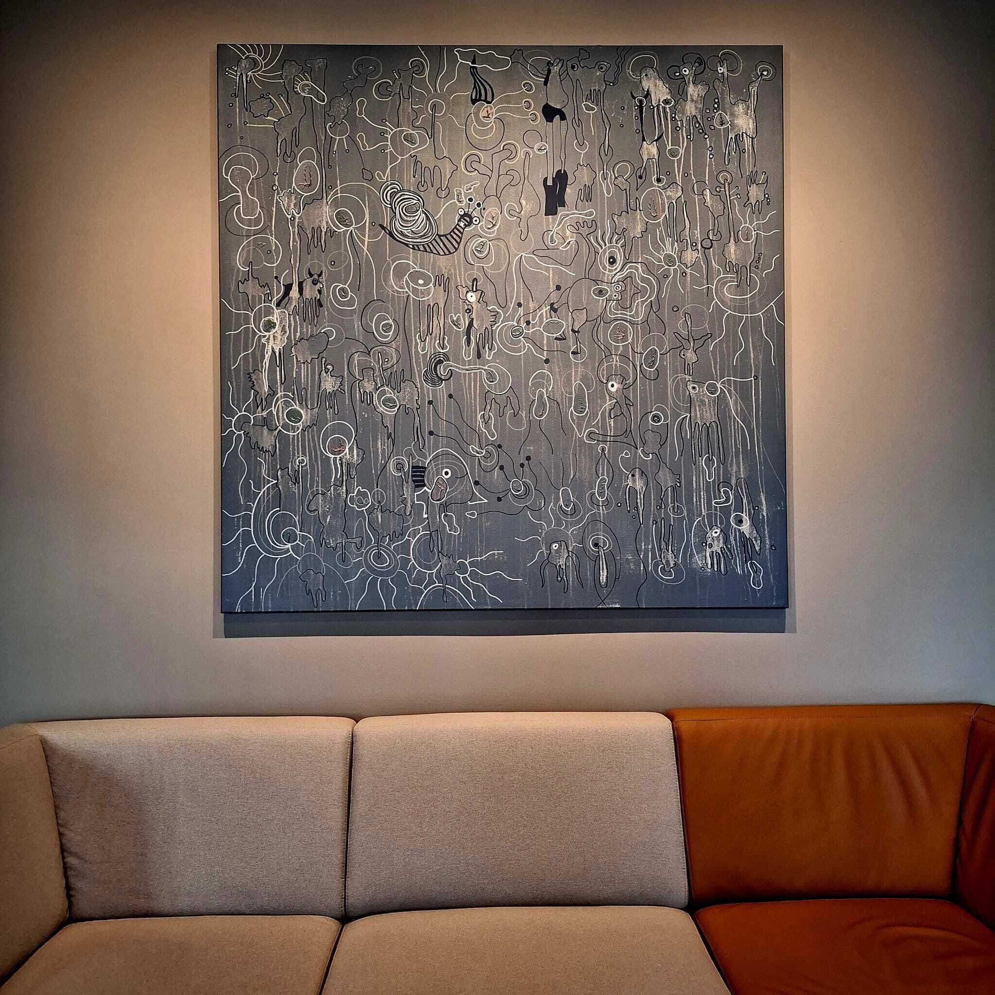 Uma sala de estar moderna com um quadro abstrato grande na parede, um sofá bege e uma almofada marrom decorativa.