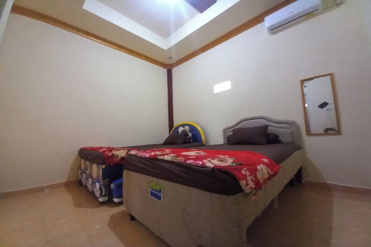 Quarto com cama, uma mesinha, uma cadeira e um ventilador de teto.