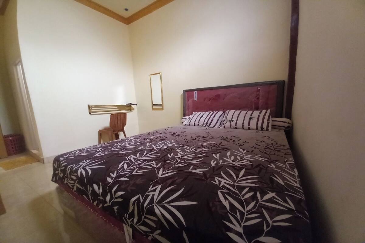 Quarto com cama, cabeceira de madeira, espelho e um banquinho.