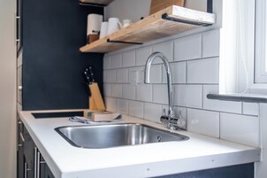 Uma cozinha moderna com pia de aço inoxidável, azulejos brancos e prateleiras de madeira acima do balcão.