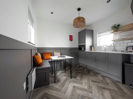 Uma cozinha moderna com armários cinza, piso de madeira em padrão herringbone, mesa de jantar branca e luminária pendente.