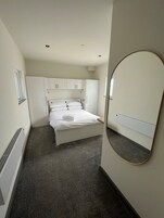 Quarto pequeno e bem arrumado com uma cama de solteiro, guarda-roupa embutido, radiador e espelho na parede.