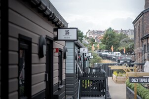 Vista da rua com edifícios numerados, um letreiro indicando '15 Red Devil' e um letreiro que diz 'COZY TAPAS'.