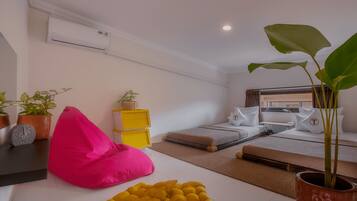 Quarto de hotel moderno com cama, um bean bag, um banquinho amarelo e uma planta em vaso.
