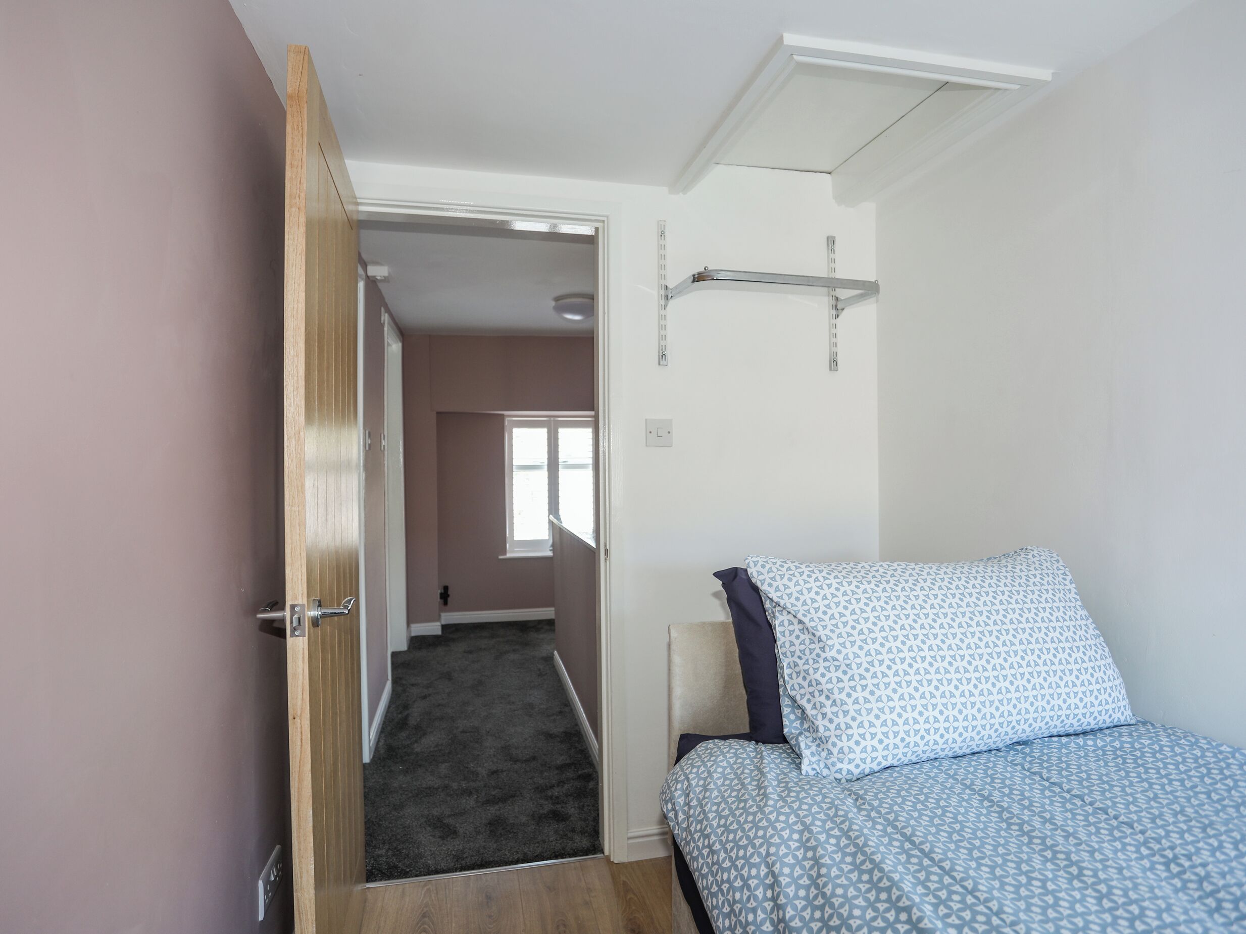 Quarto com cama, mesa de cabeceira, janela e porta que dá para outro espaço.