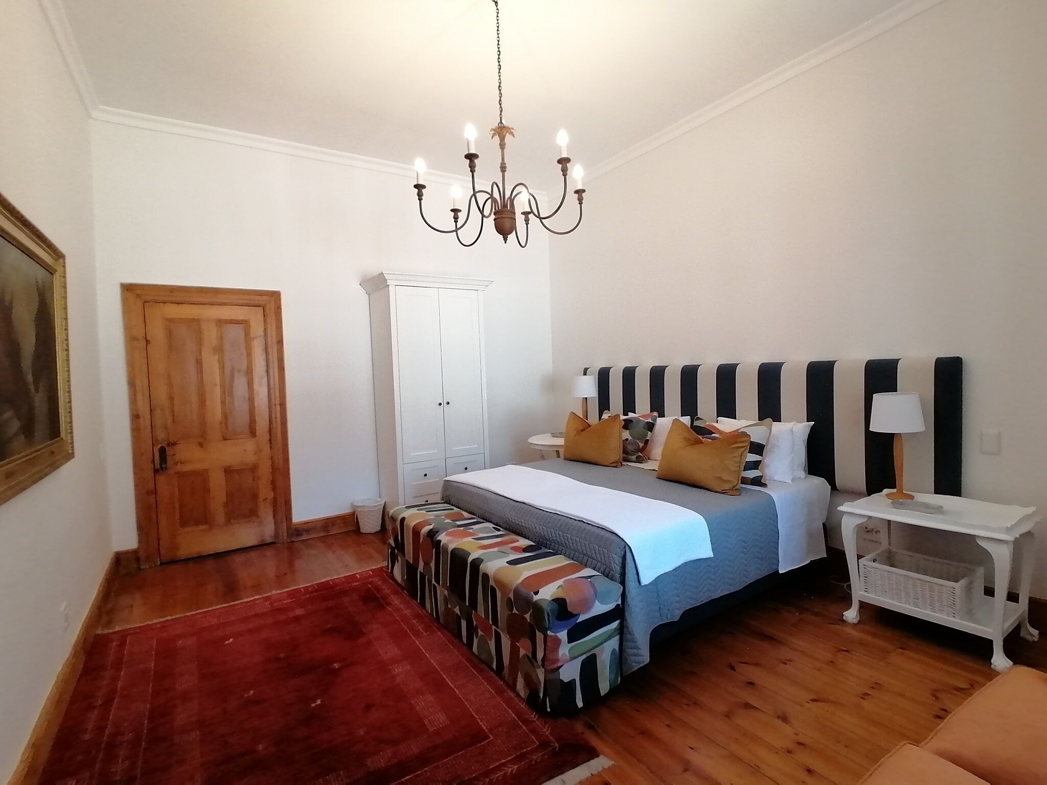 Quarto com cama, lustre, guarda-roupa, mesa de cabeceira e tapete vermelho.