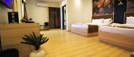 Quarto de hotel com piso de madeira, duas camas, uma TV e um vaso de planta.
