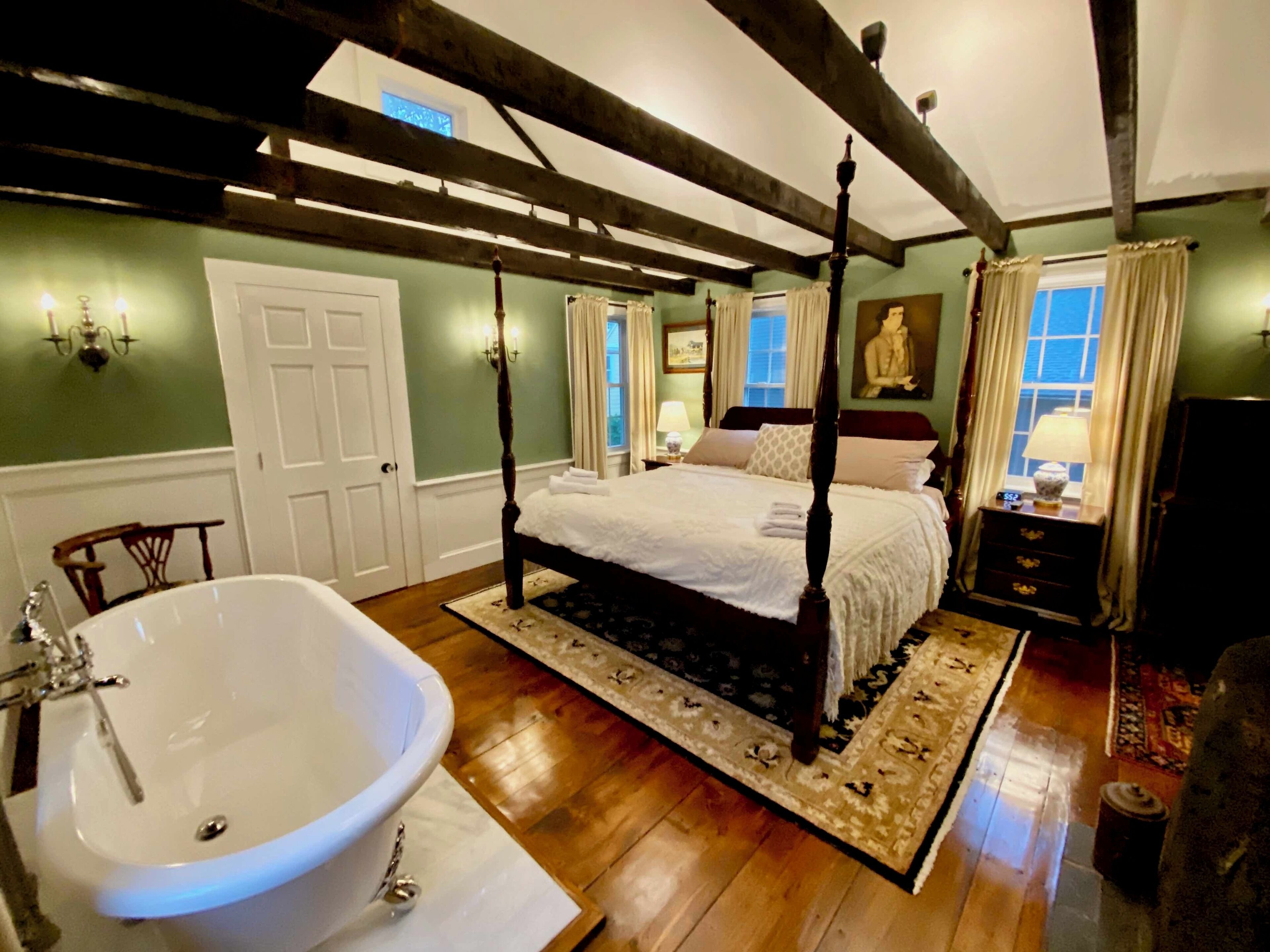 Quarto com cama de dossel, uma banheira grande e piso de madeira.