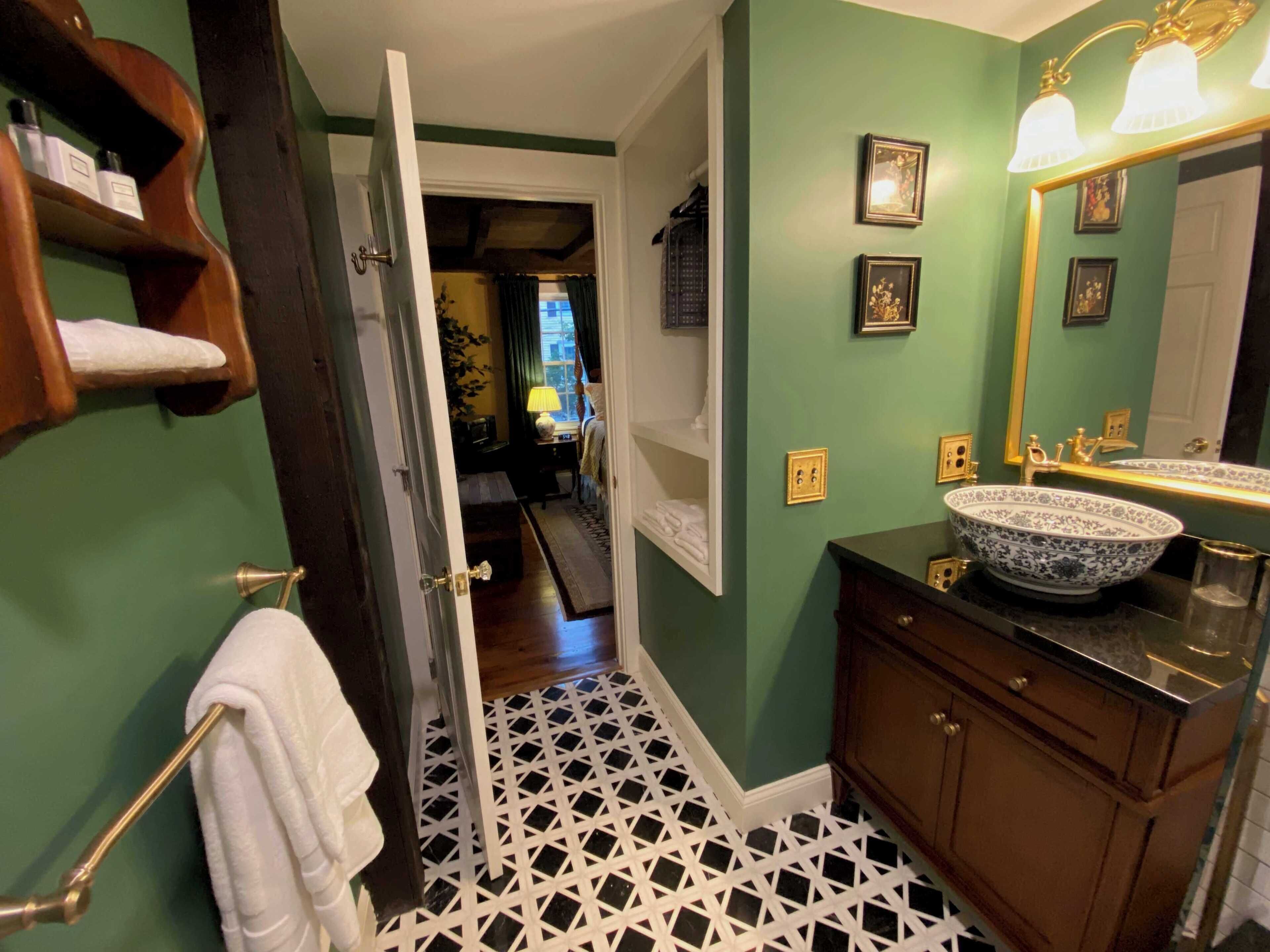 Um banheiro com piso em padrão preto e branco, pia branca com uma tigela decorativa e espelho com moldura dourada.