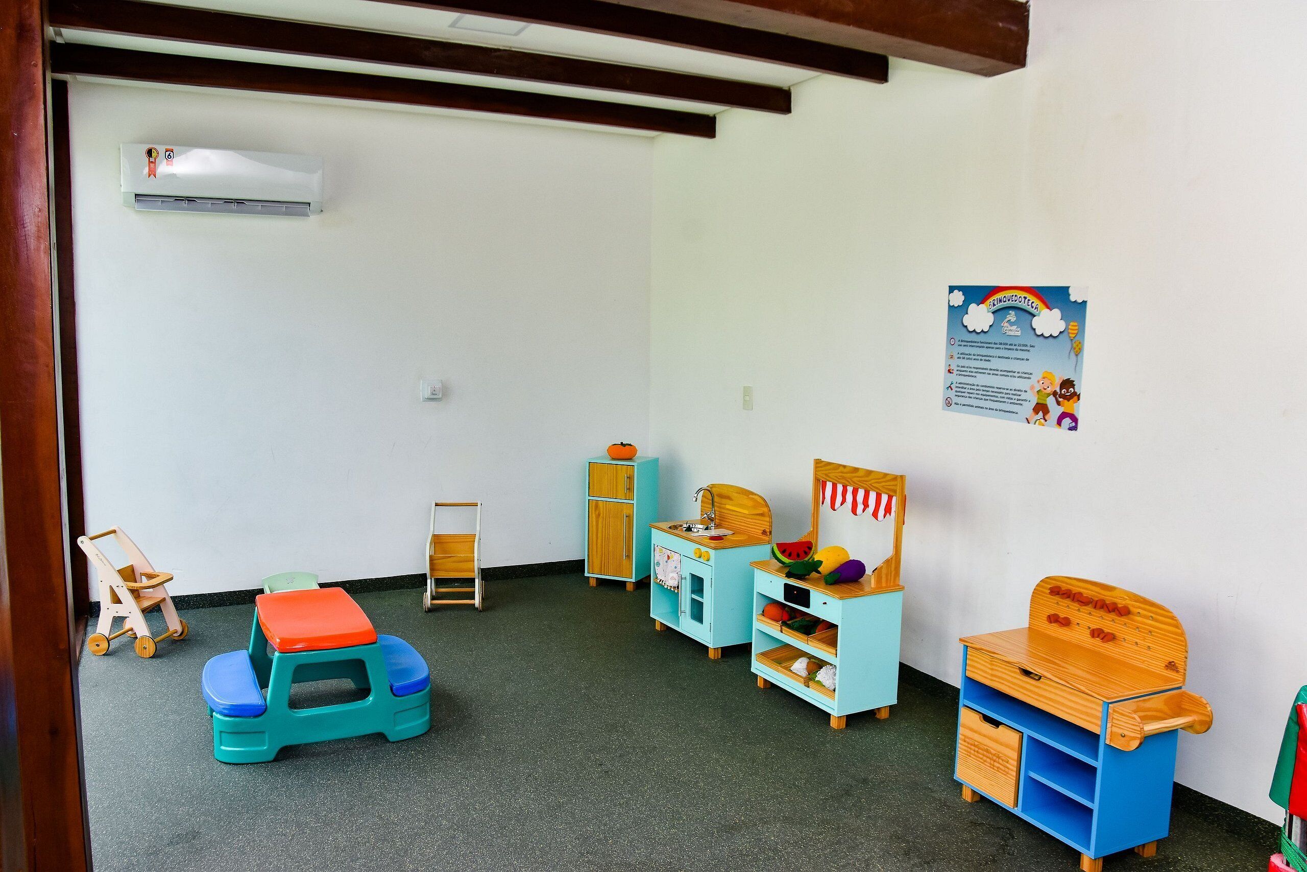 Uma sala de brinquedos infantil com uma pequena mesa, um carrinho de brinquedo e um conjunto de cozinha de brinquedo.