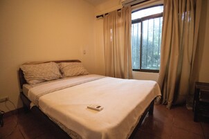 Cama bem arrumada em quarto com janela e cortinas.