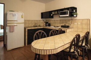 Uma cozinha compacta com geladeira, micro-ondas e uma pequena mesa de jantar com cadeiras.