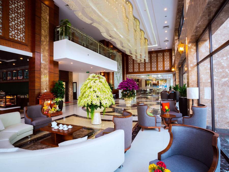 Um hall amplo com teto alto, área de estar com sofás e poltronas, um grande arranjo floral e vista do interior do hotel.