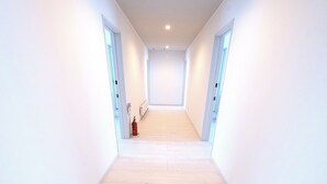 Um corredor estreito, bem iluminado, com piso de madeira clara e paredes brancas.