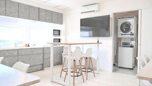 Uma cozinha moderna com ilha central, banquetas, micro-ondas embutido e televisão montada na parede.