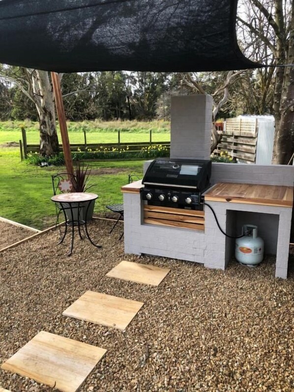 Uma área de churrasco ao ar livre com fogão a gás, mesa e churrasqueira.