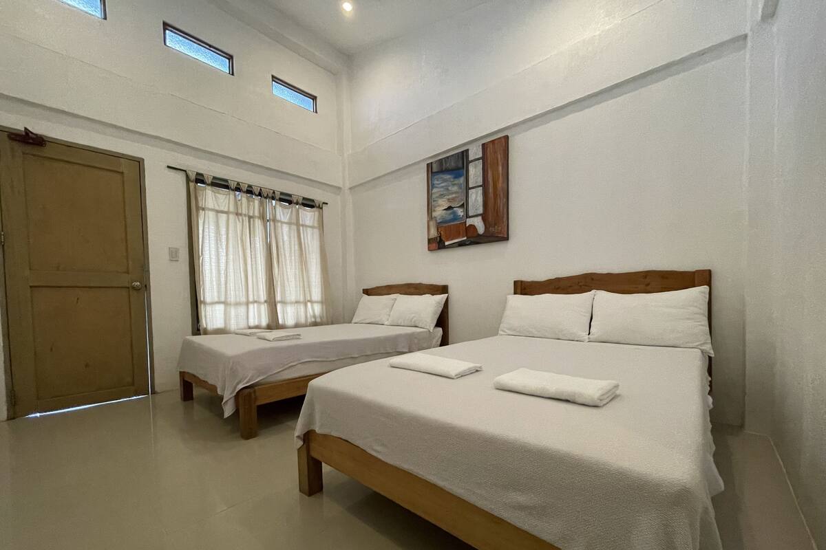 Quarto de hotel com duas camas, uma porta de madeira, uma janela com cortinas e um quadro na parede.