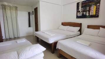 Quarto de hotel com três camas, uma grande pintura abstrata na parede e uma janela com cortinas.