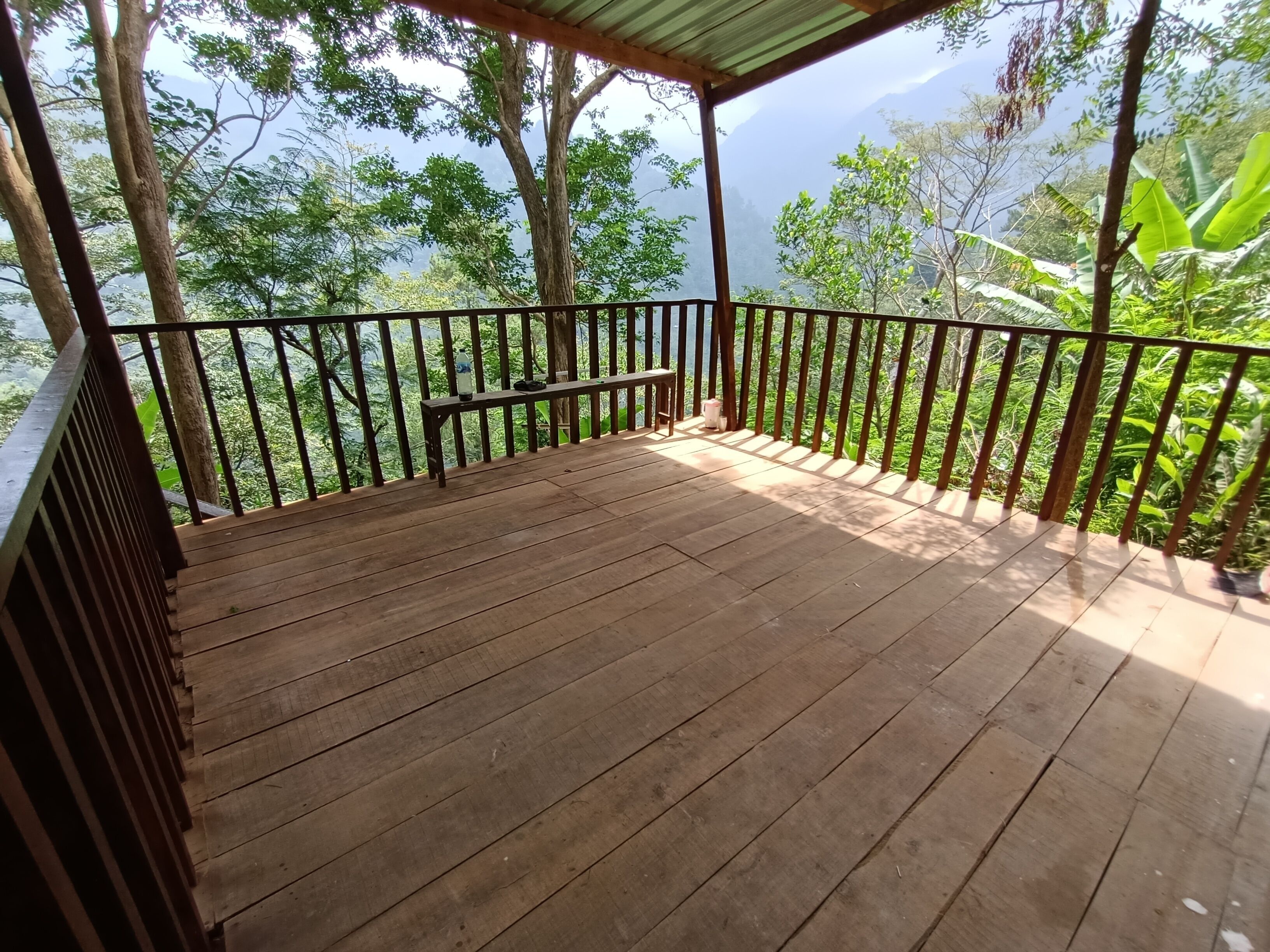 Um deck de madeira com guarda-corpo de metal, um banco e um vaso com planta.