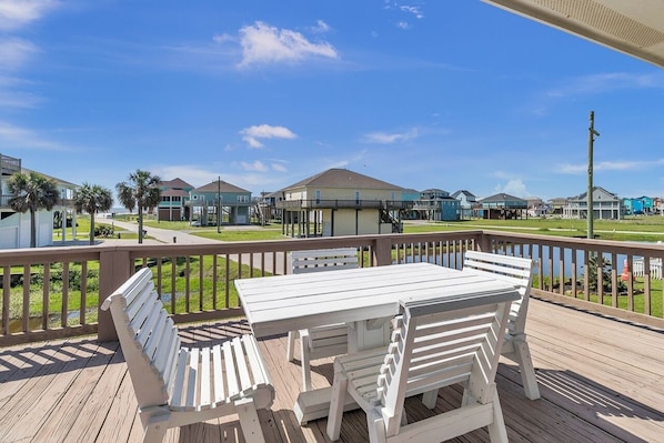 Um deck de madeira com mesa e bancos, com vista para uma área residencial com casas e um corpo de água.