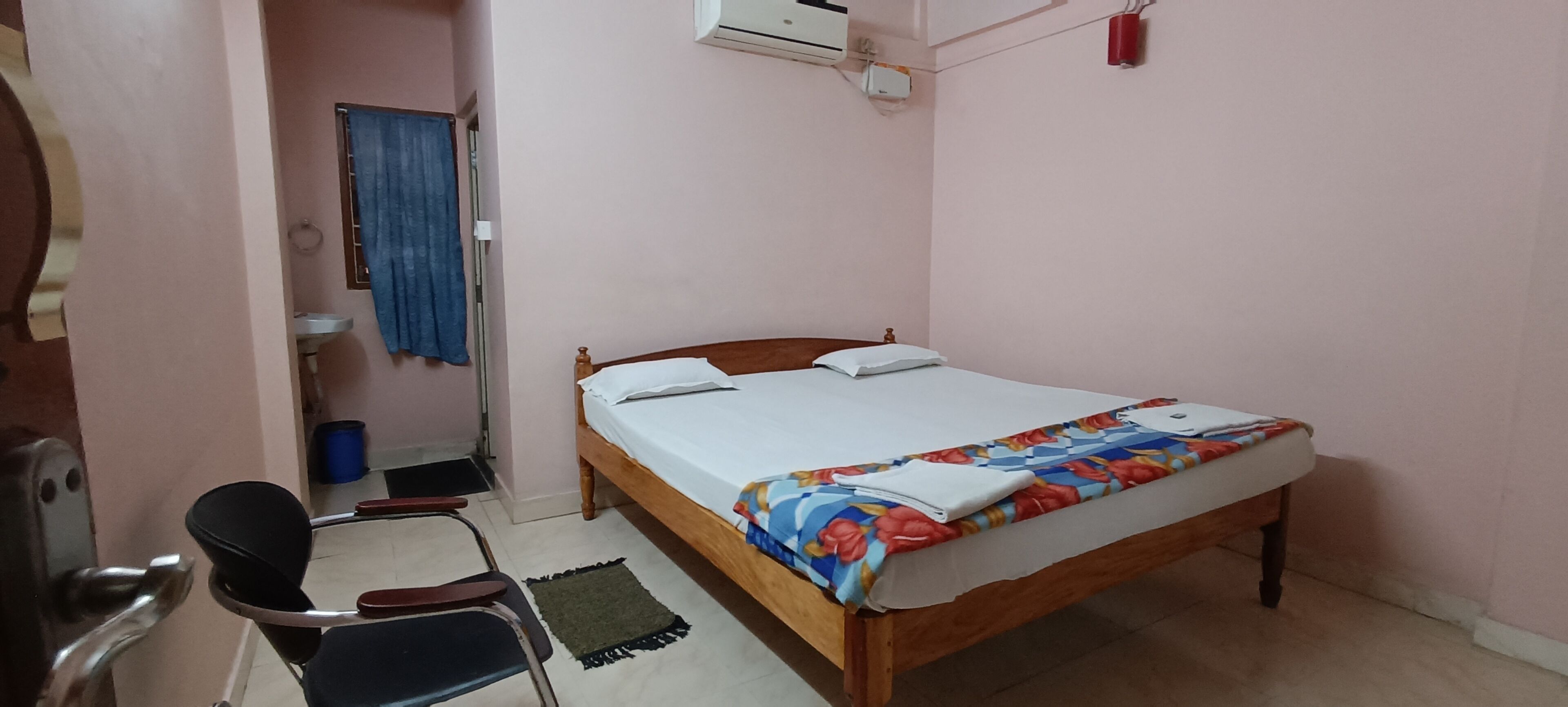 Quarto com cama, cadeira, escrivaninha e janela com cortina.