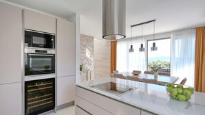 Uma cozinha moderna com eletrodomésticos embutidos, um espaço de refeições com mesa e cadeiras, e vista através de grandes janelas.