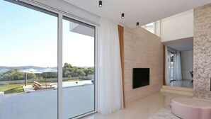 Uma sala de estar moderna com uma grande porta de vidro deslizante que dá para uma área externa, uma televisão de tela plana na parede e um banquinho rosa.