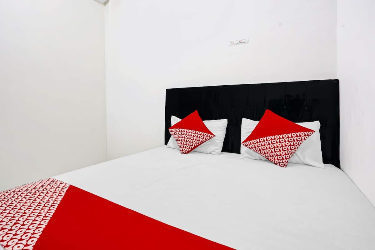 Quarto de hotel com cama branca, cabeceira preta e almofadas com padrão vermelho e branco.