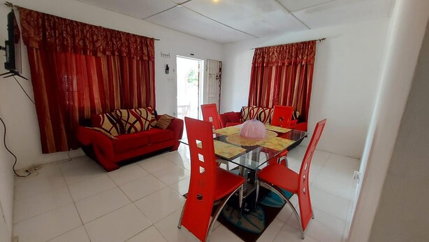 Uma área de refeições com mesa de vidro, cadeiras vermelhas e sofá vermelho.