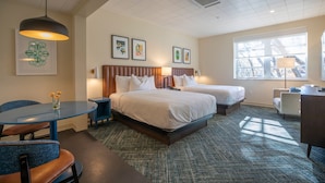Quarto de hotel com duas camas, uma escrivaninha, uma cadeira e obras de arte nas paredes.