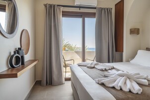 Quarto de hotel com uma cama, uma mesinha, uma cadeira e vista para o mar através de janelas amplas.