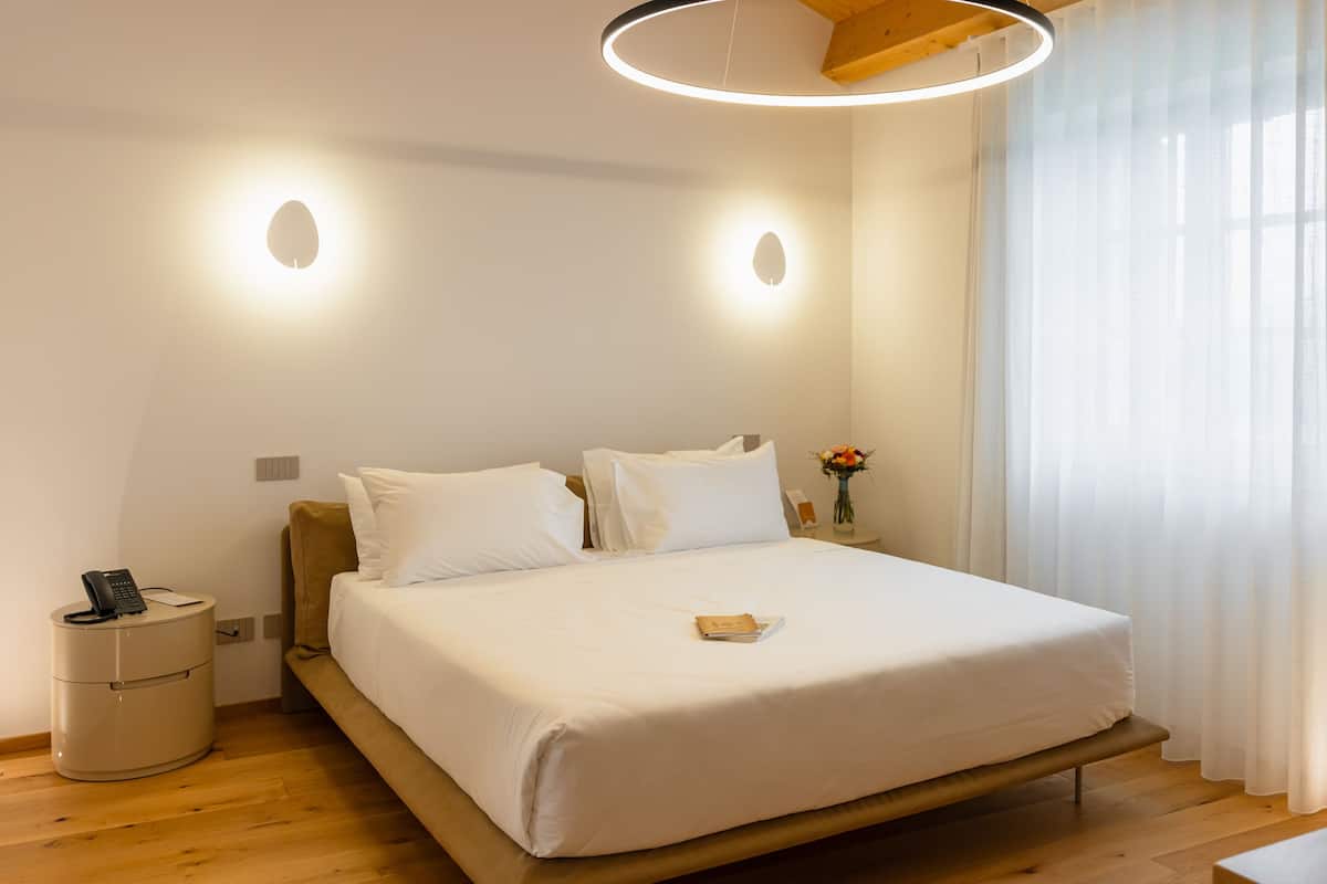 Quarto moderno com cama de madeira, roupa de cama branca, mesa de cabeceira com um telefone e um vaso de flores.