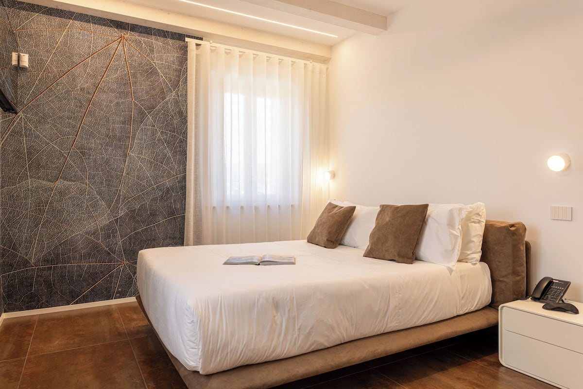 Quarto moderno com cama grande, mesa de cabeceira e luminária na parede.