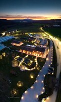 Vista aérea de um grande complexo de edifícios com várias estruturas, área de estacionamento e jardins ajardinados ao anoitecer.