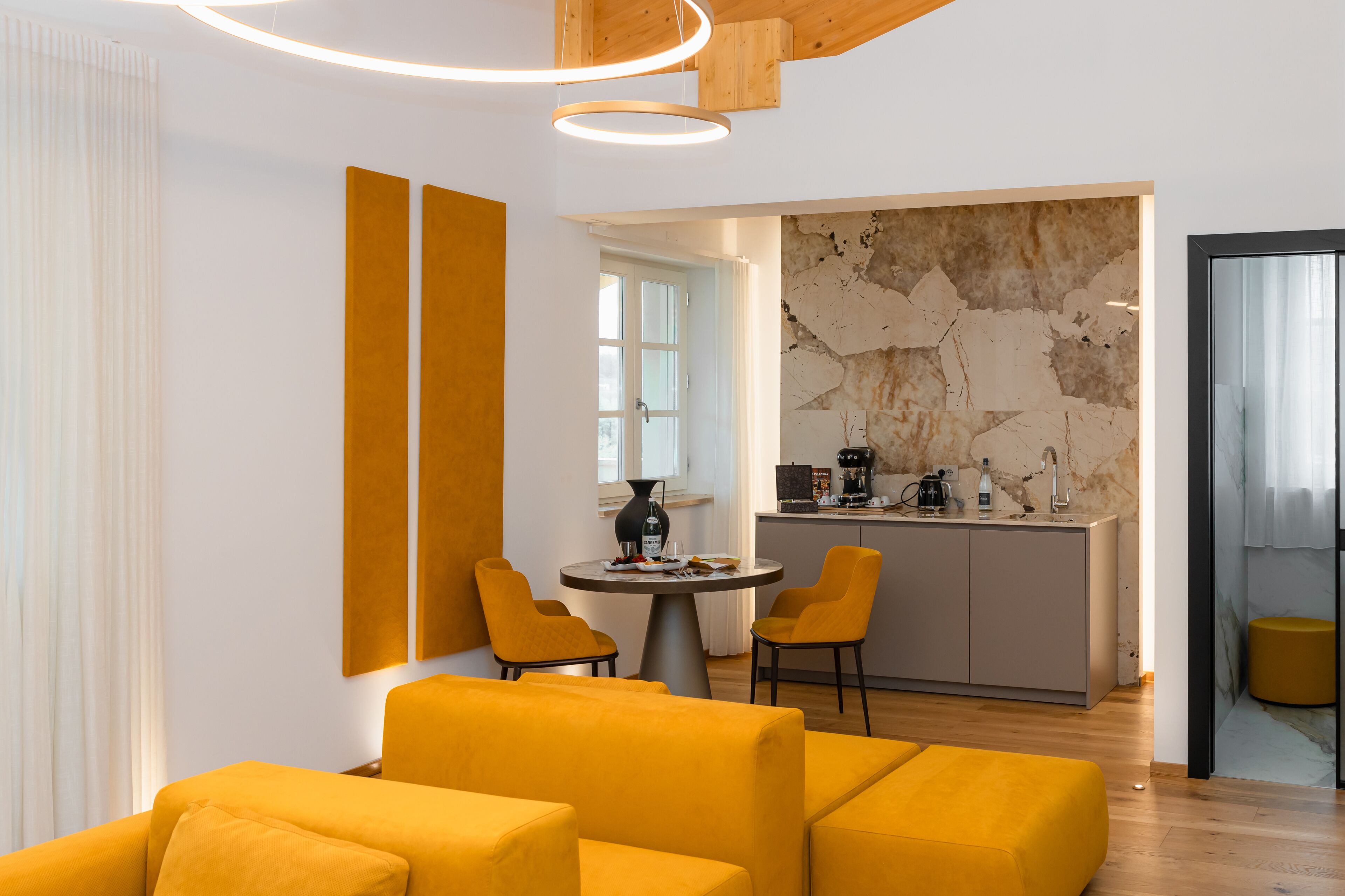 Uma sala de estar moderna com sofás amarelos, uma mesa redonda e uma área de cozinha com painel de mármore.