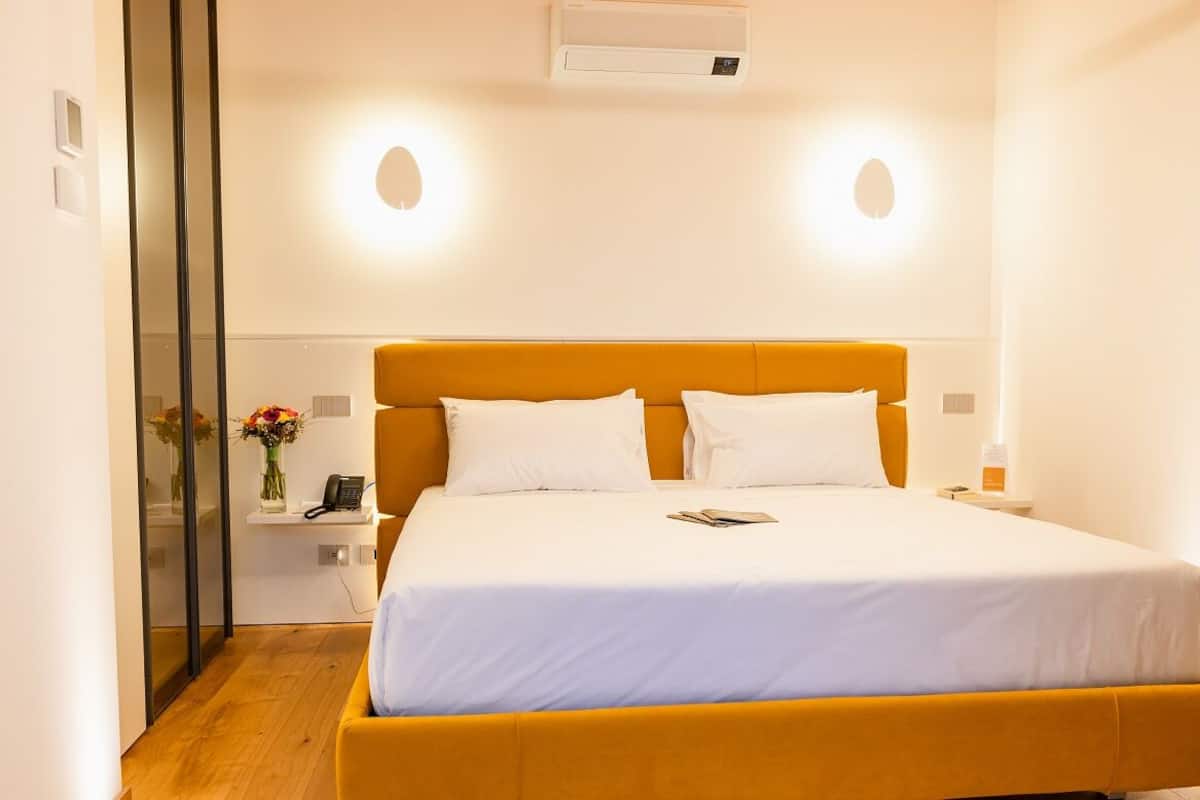 Quarto de hotel com cama grande, mesas de cabeceira, espelho e ar condicionado fixado na parede.