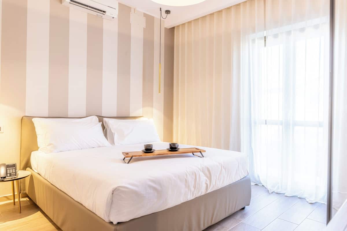 Quarto de hotel com uma cama grande, mesa de cabeceira com telefone e bandeja com duas chávenas.
