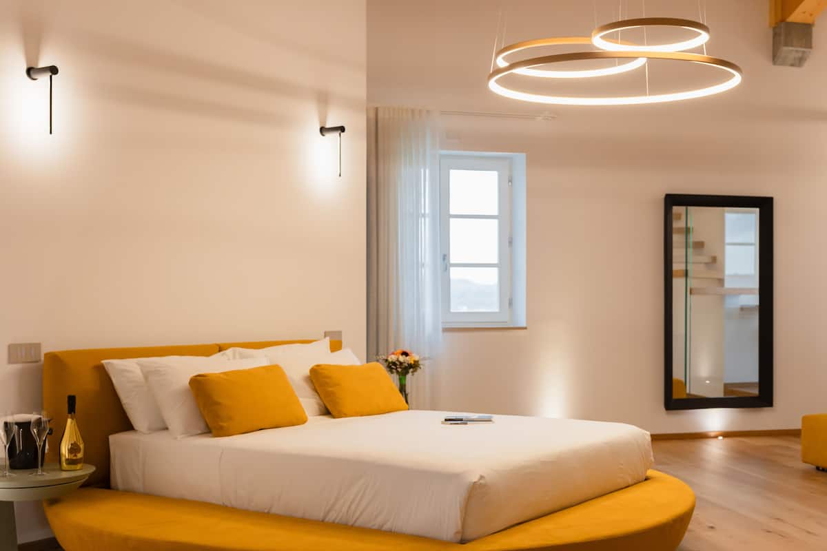 Quarto moderno com cama curva, luminária redonda e um espelho grande.
