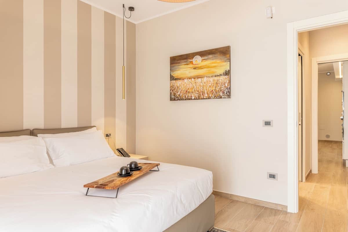 Um quarto com cama, um quadro, uma mesa de cabeceira e um criado-mudo.