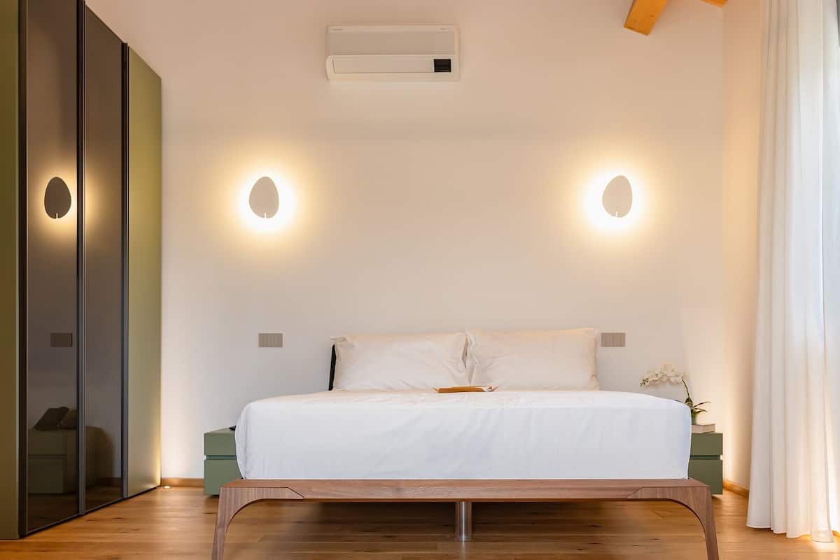 Quarto moderno com uma cama no centro, ladeada por duas luminárias fixadas na parede.