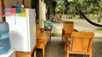 Uma área de estar coberta ao ar livre, com um bebedouro, geladeira e uma mesa e cadeiras de madeira.