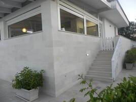 Um edifício moderno com escadaria que leva a uma varanda, janelas amplas e plantas em vasos.