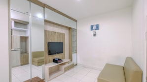 Uma sala de estar moderna com televisão de tela plana, um sofá bege, uma divisória de vidro e um armário de madeira.