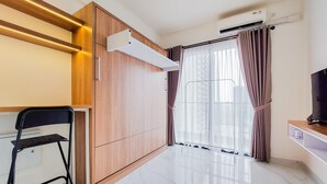 Quarto moderno com guarda-roupa de madeira, uma cadeira preta, TV sobre suporte de madeira e uma janela grande com cortinas.