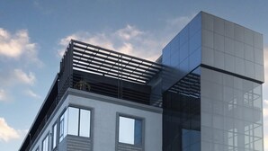 Um edifício moderno com fachada de vidro, grandes janelas e telhado plano com estrutura metálica.