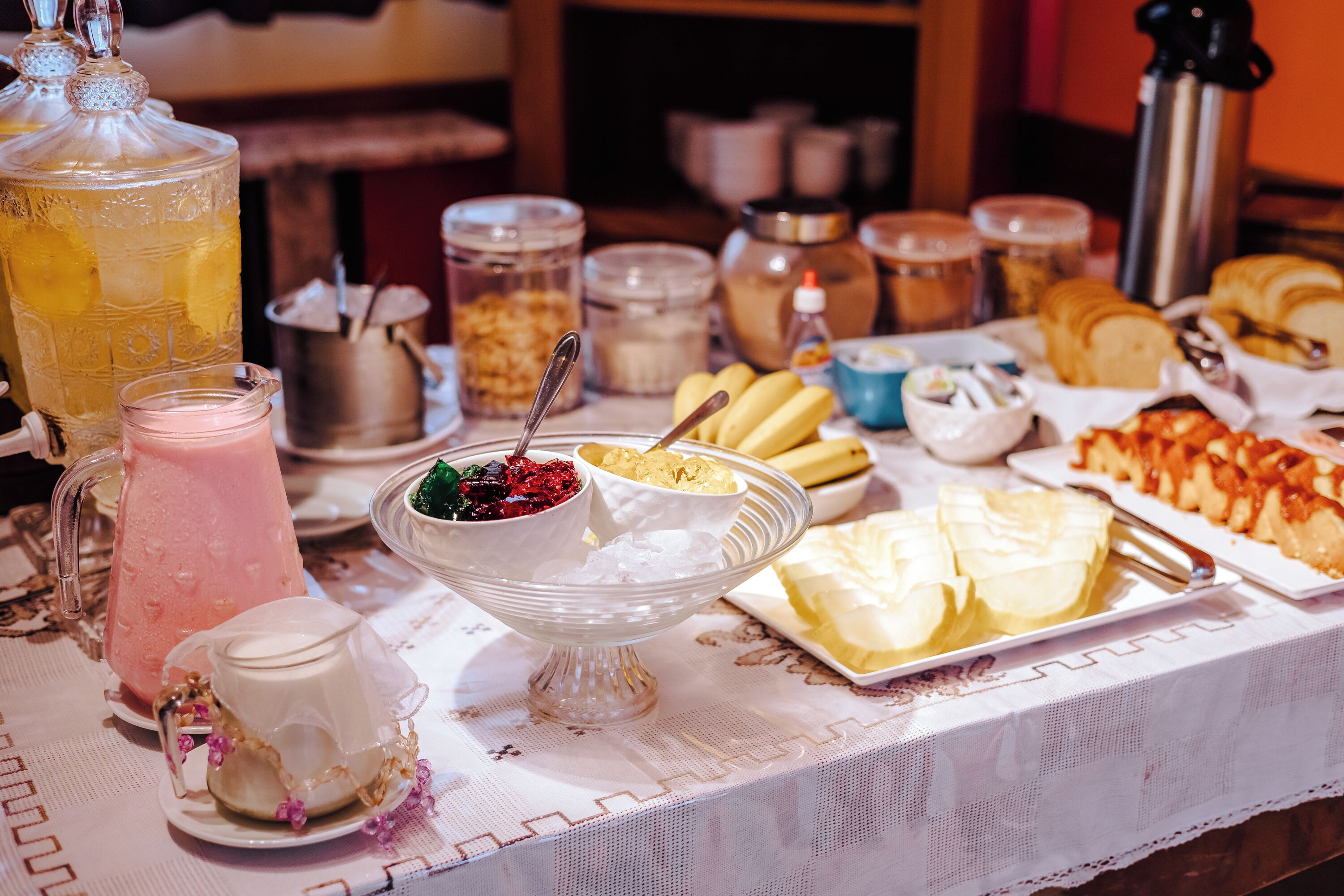 Buffet de café da manhã com diversos alimentos, incluindo frutas, doces e bebidas.