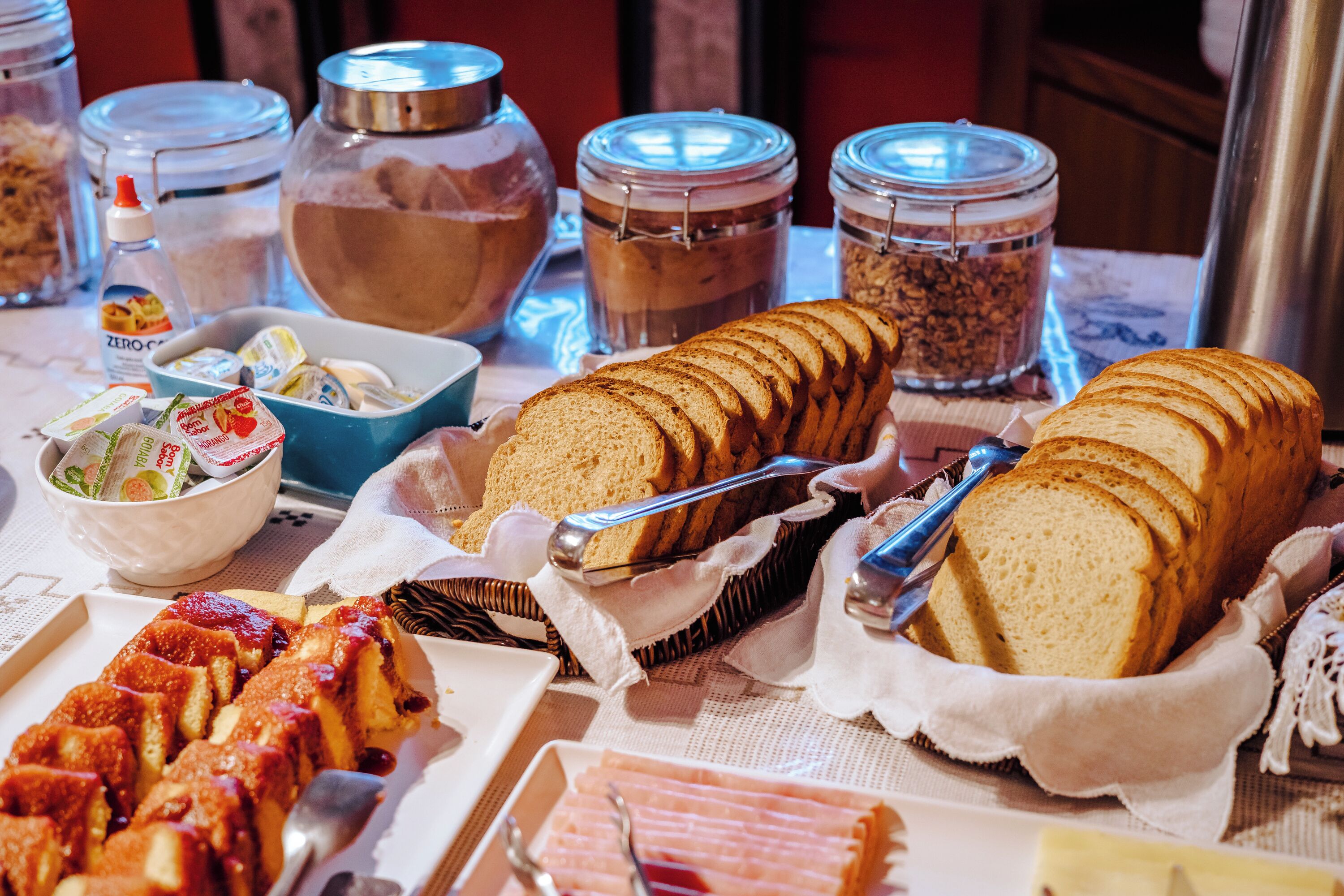 Uma mesa de buffet com diversos alimentos, incluindo pão, iogurte e sobremesa.