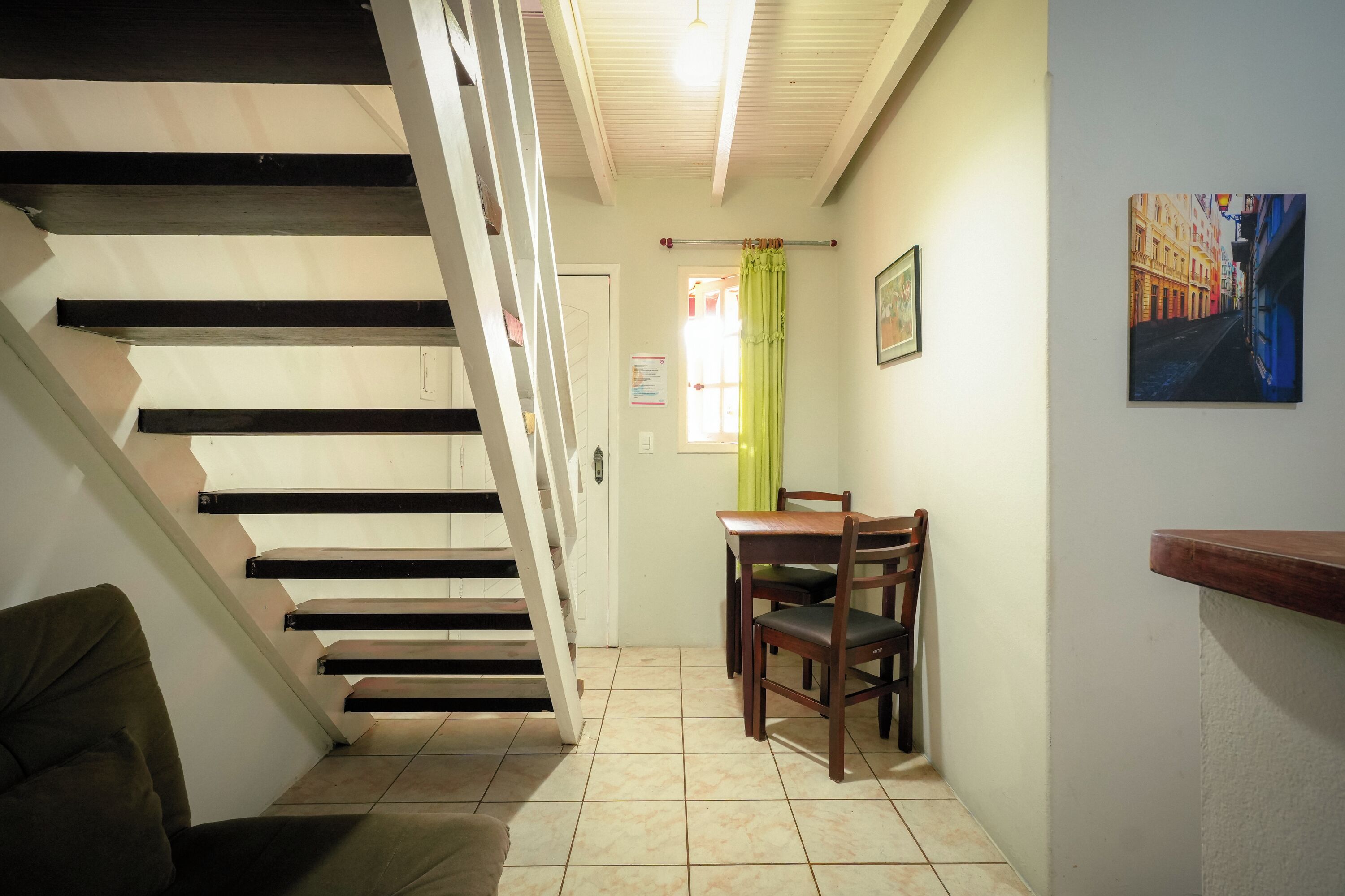 Uma escada com corrimão, uma sala de jantar com mesa e cadeiras, e um quadro na parede.