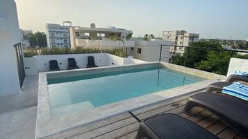 Uma área de piscina no terraço, com espreguiçadeiras e vista ampla dos edifícios ao redor.